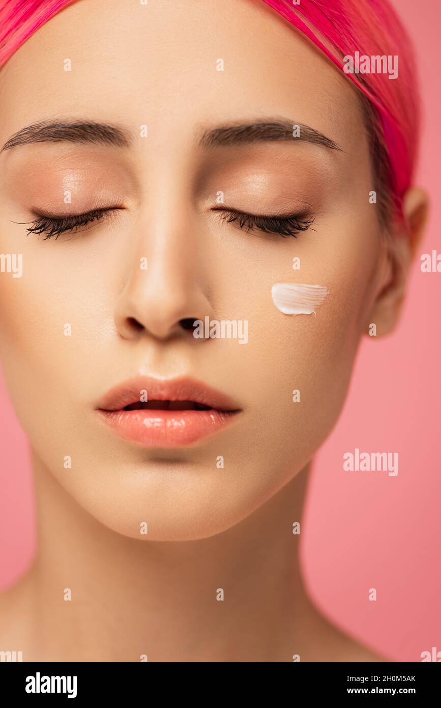 close up of young woman with closed eyes and face cream on cheek ...