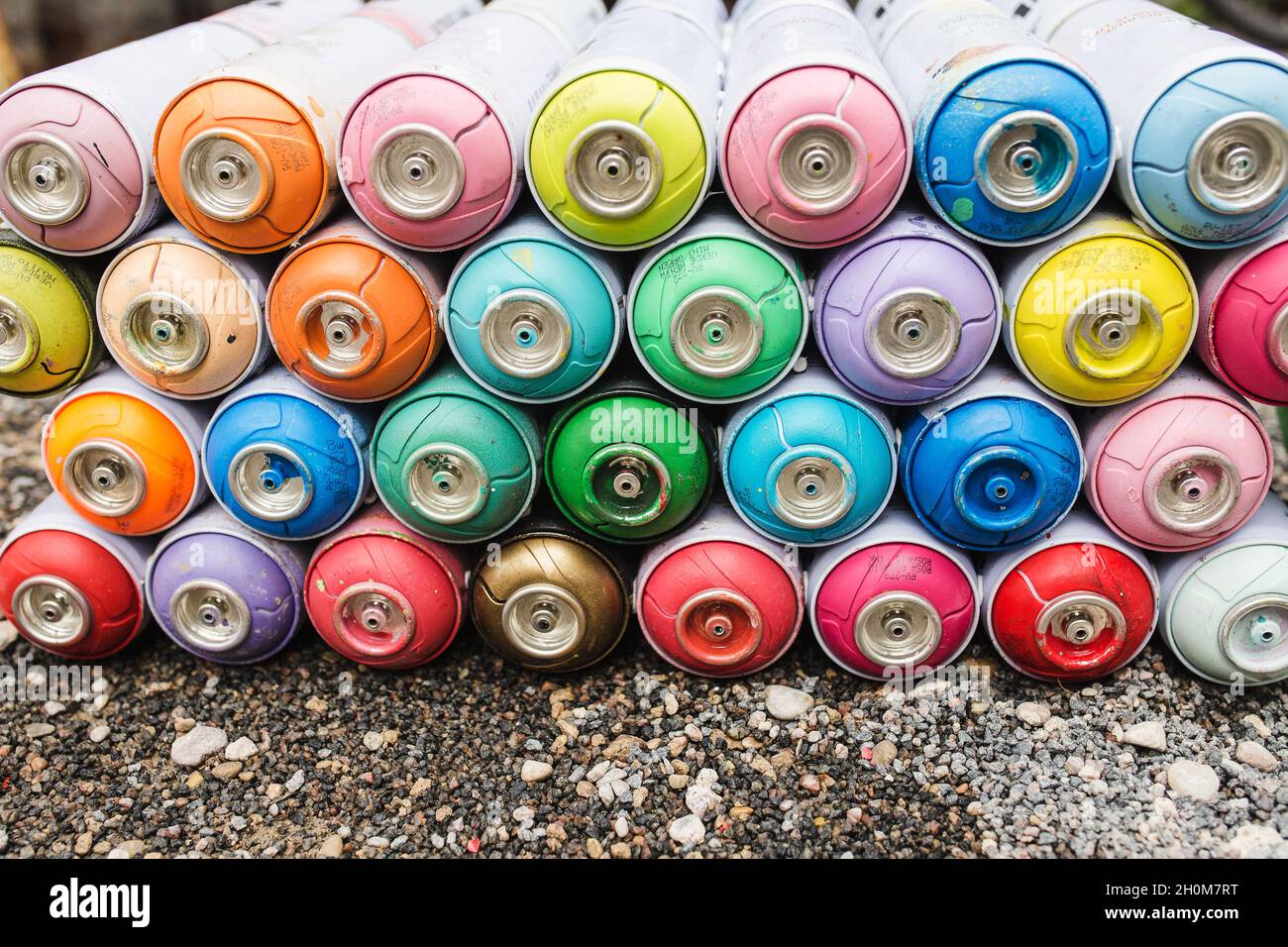 Paint spray cans with multi-colored round lids lie in rows as a pattern ...