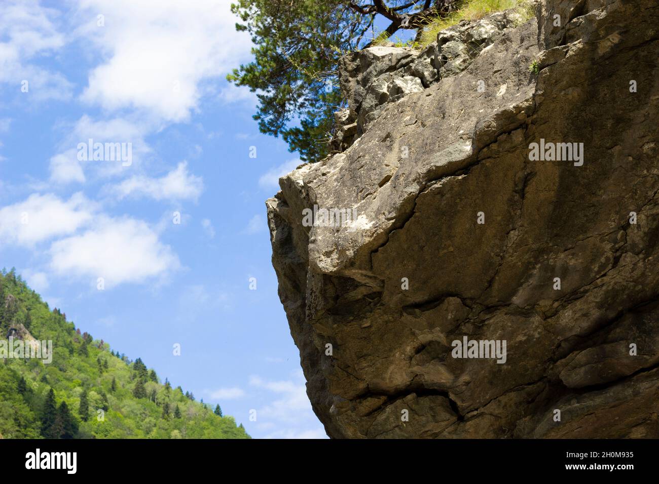 Trees and grass grow on the rock. In background blue sky with clouds ...