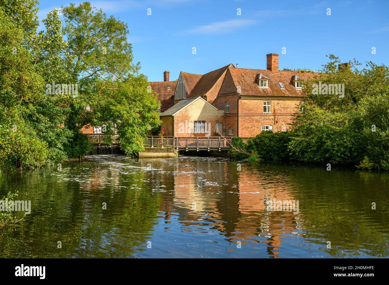 The red brick buildings of Flatford Mill viewed from across river Stour ...