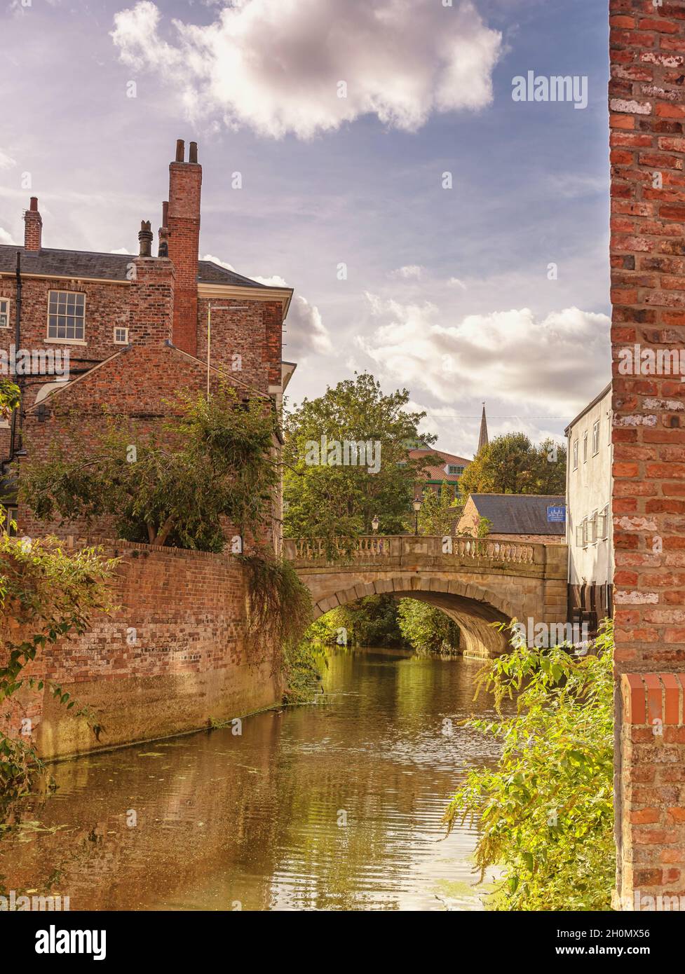 An old bridge spans a river. An old brick building is to one side and a ...