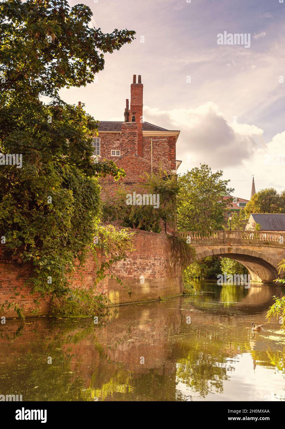 An old bridge spans a river. An old brick building is to one side and a ...