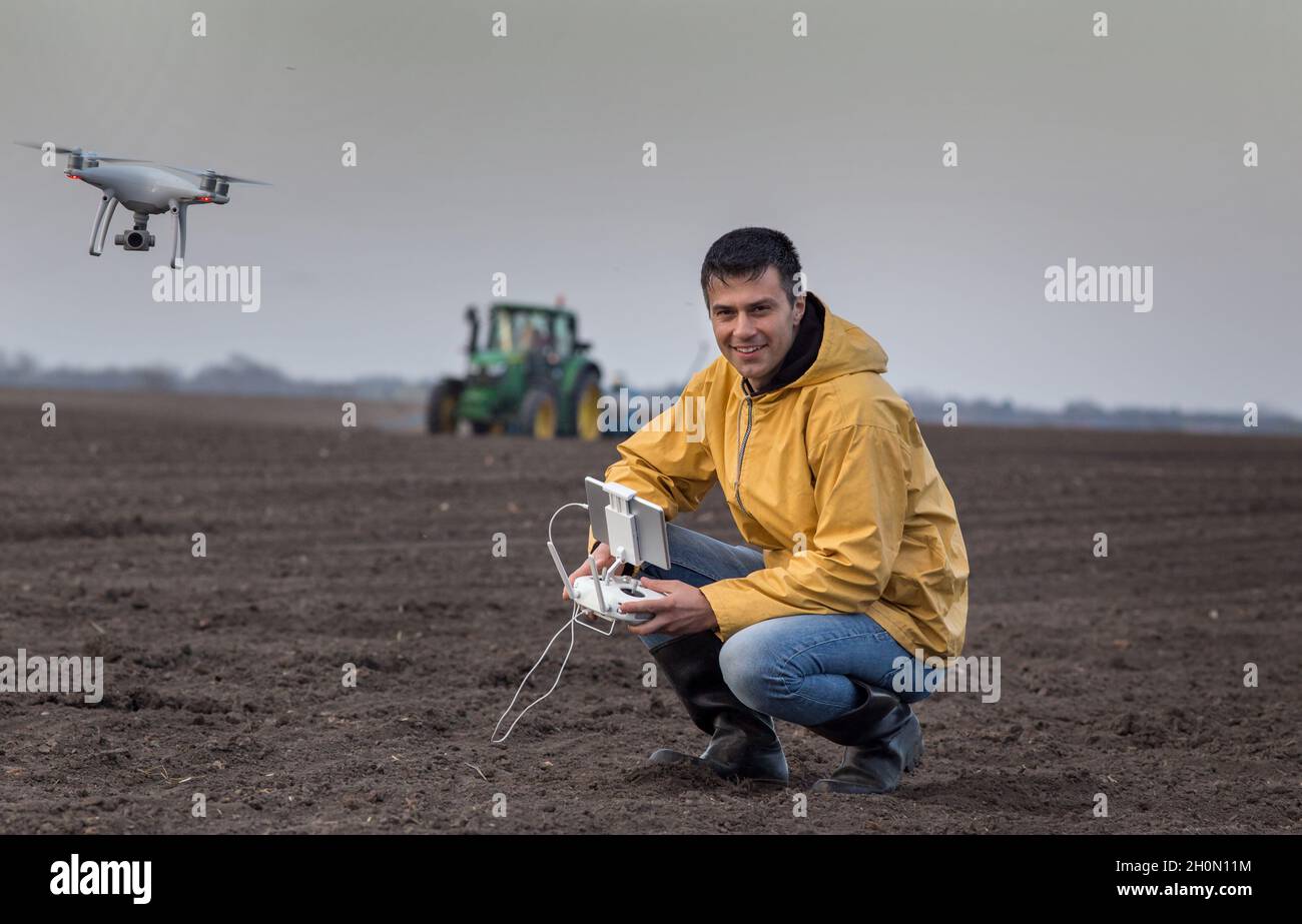 Attractive farmer navigating drone above farmland. Tractor working in ...