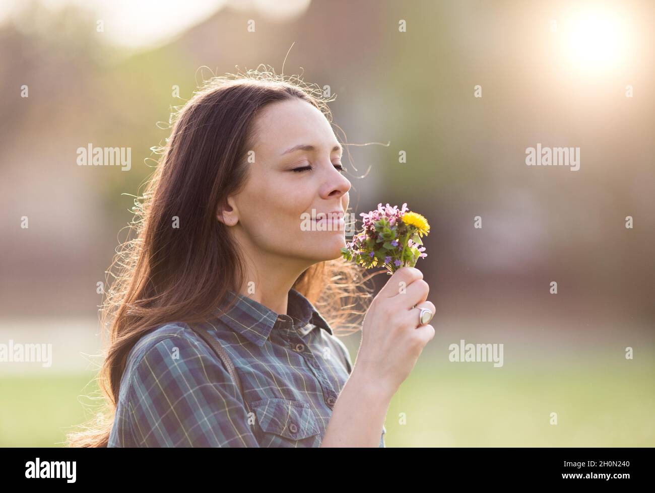 Pretty young woman smelling field flowers in park. Peaceful and special ...