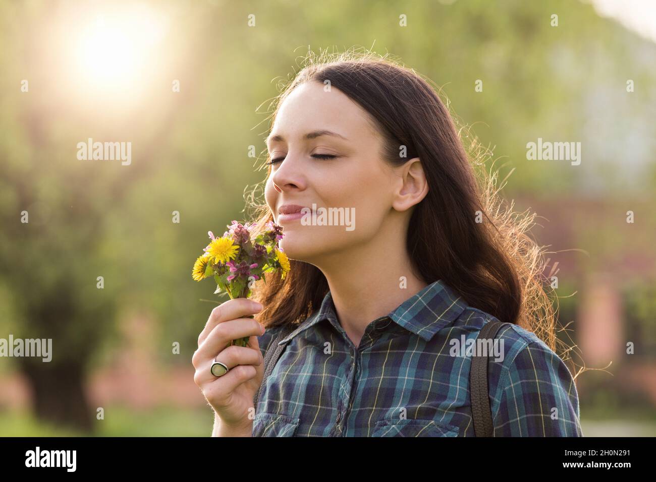 Pretty young woman smelling field flowers in park. Peaceful and special ...
