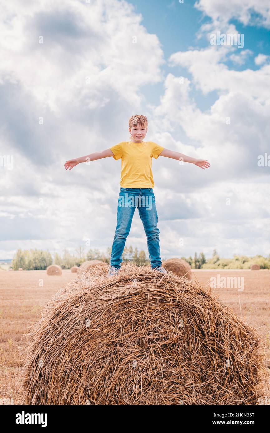 Little cute red-haired farmer boy on a stack in a field on a hot day ...