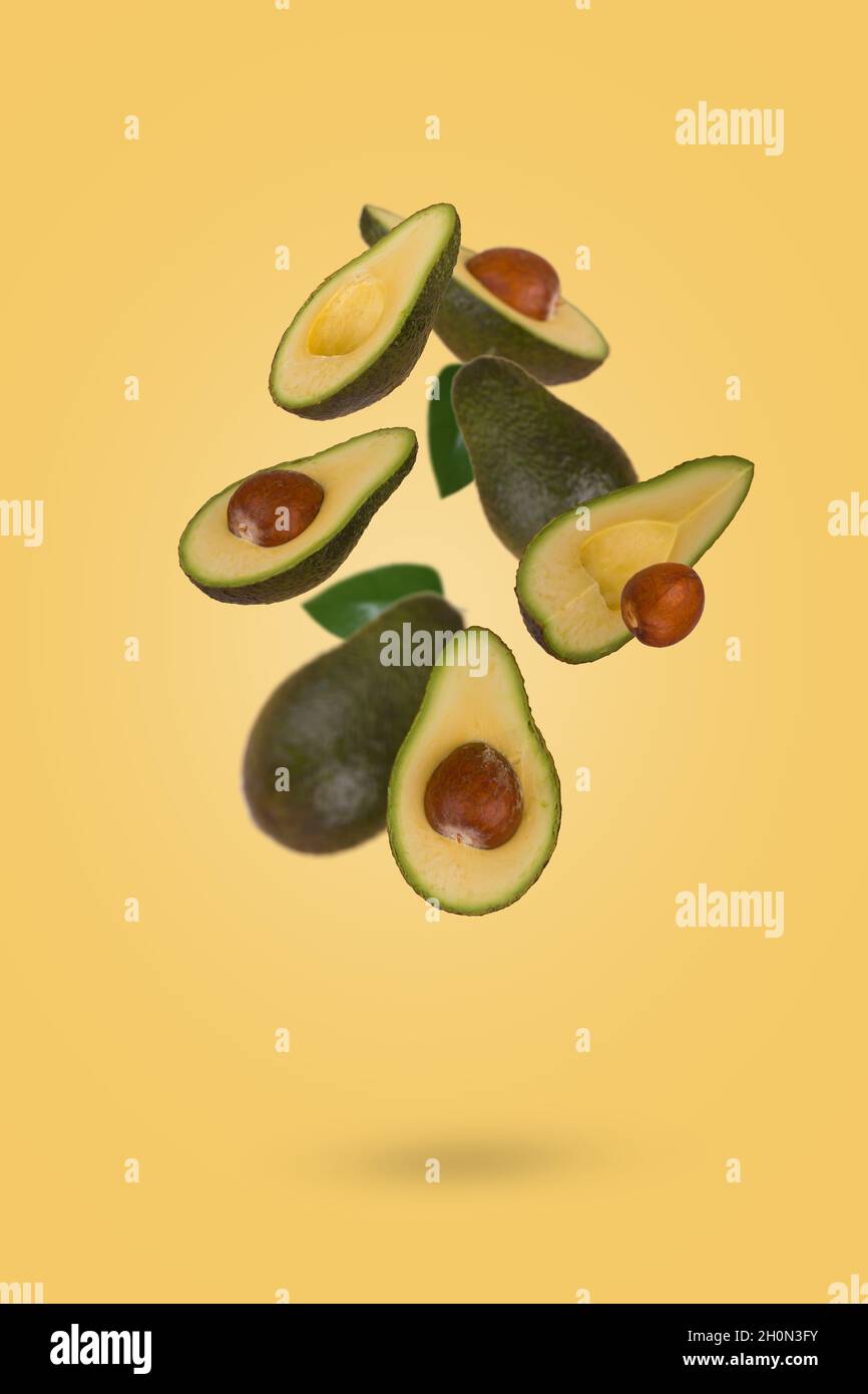 Fresh whole and sliced avocado flying in air isolated on pastel yellow ...