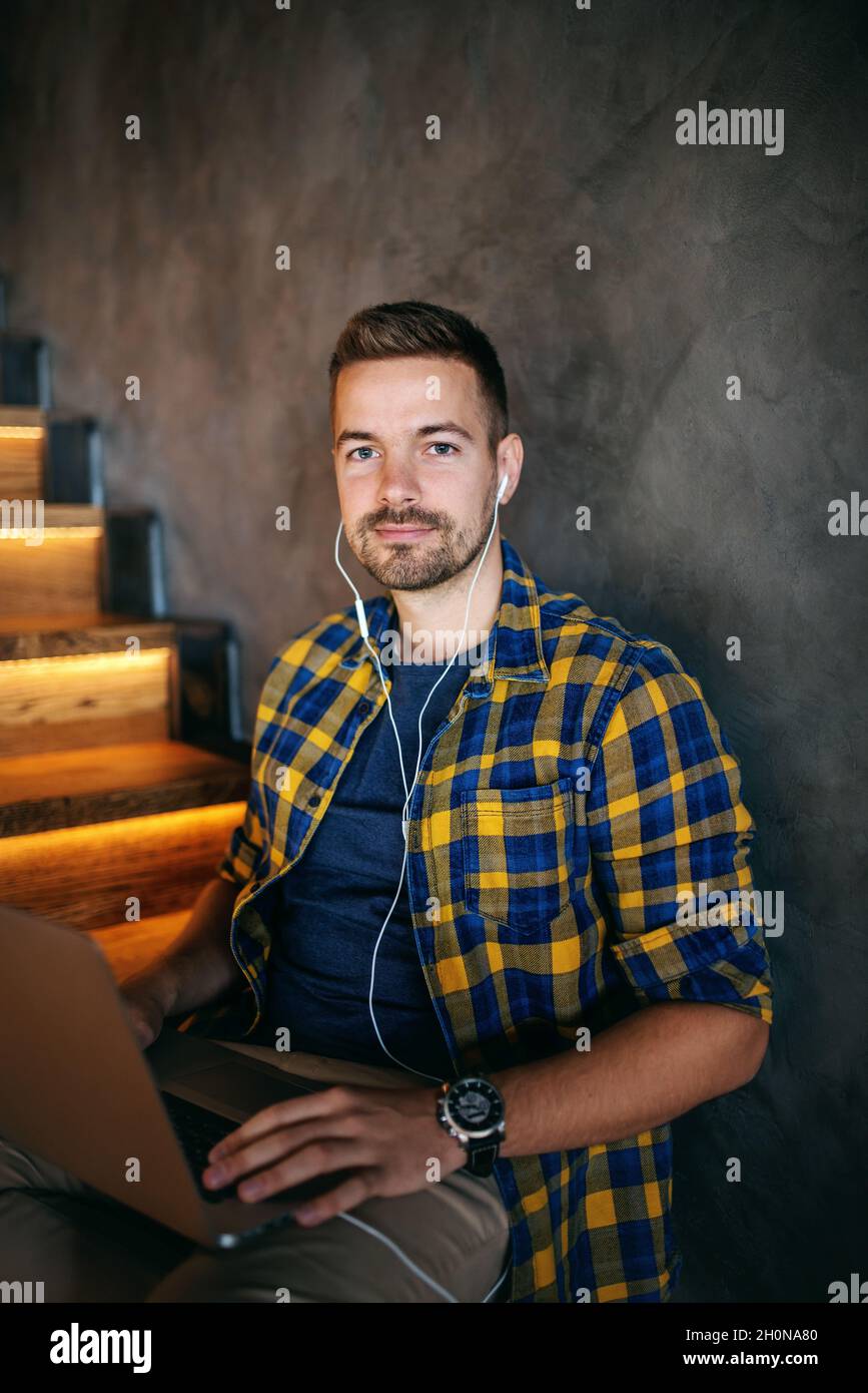 Smiling young man chilling at coffee shop sitting on stairs, surfing on ...