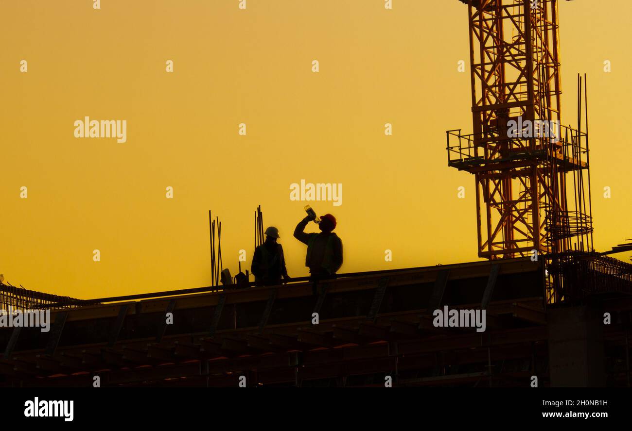 Construction worker drinking water from bottle on building site with crane in background Stock ...