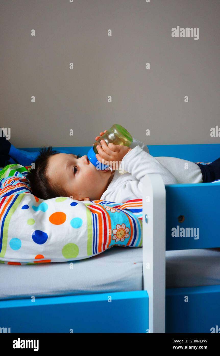 Cute little boy laying on the bed and drinking juice in the ...