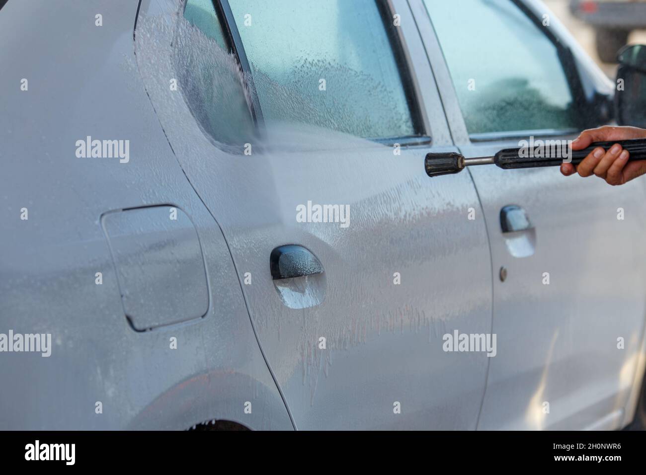 hand with high pressure washer washing white car at public self service ...