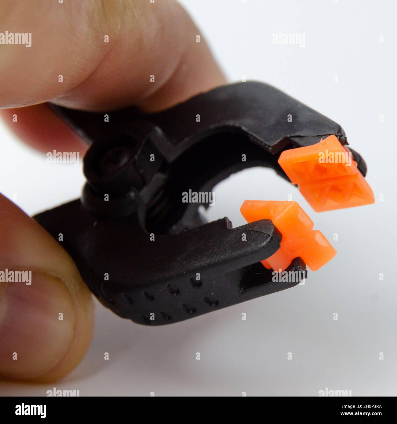 A black and orange spring clip is unclenched in the hand between the ...