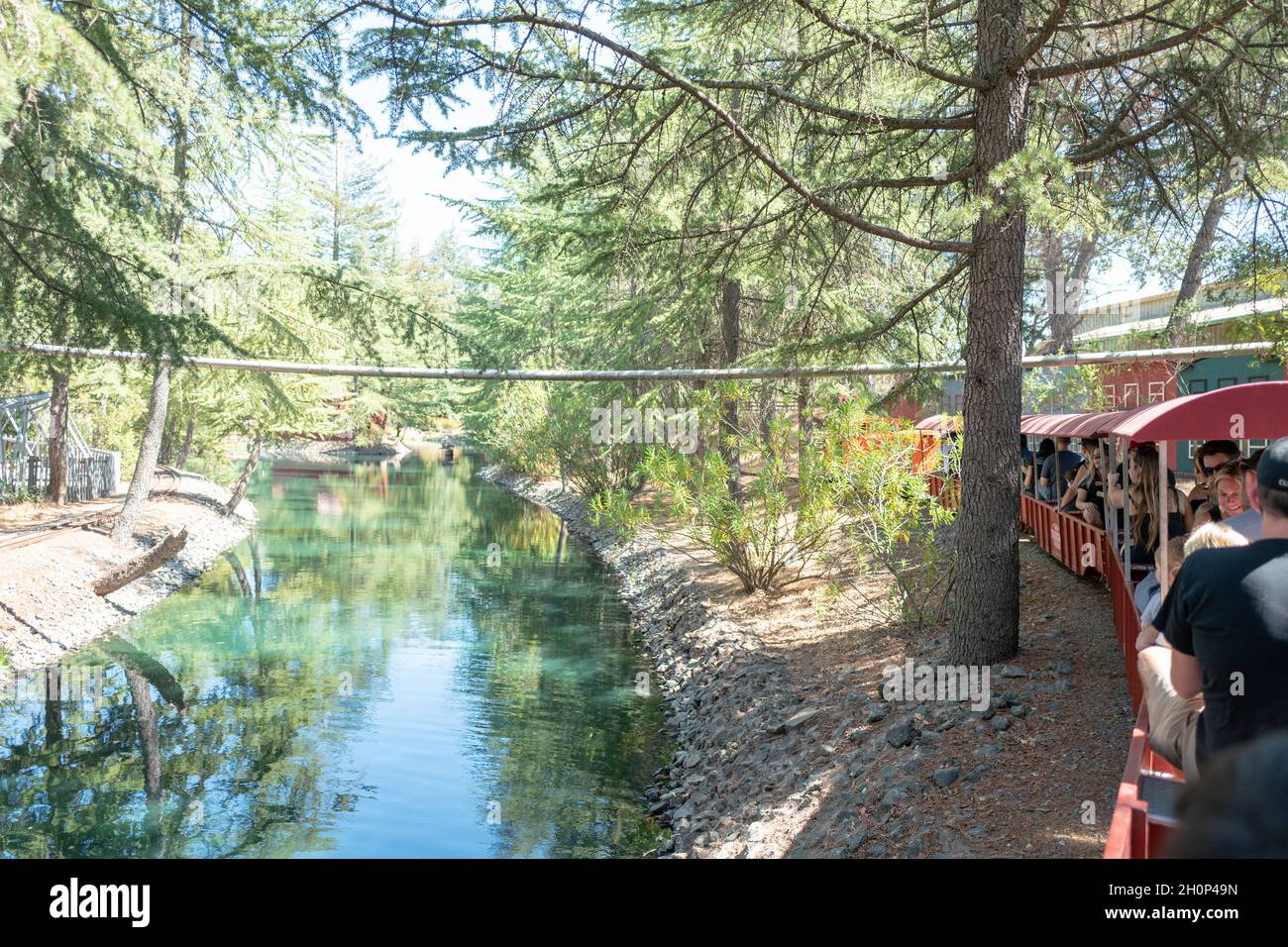 People ride a small gauge railroad train past an artificial lake at ...