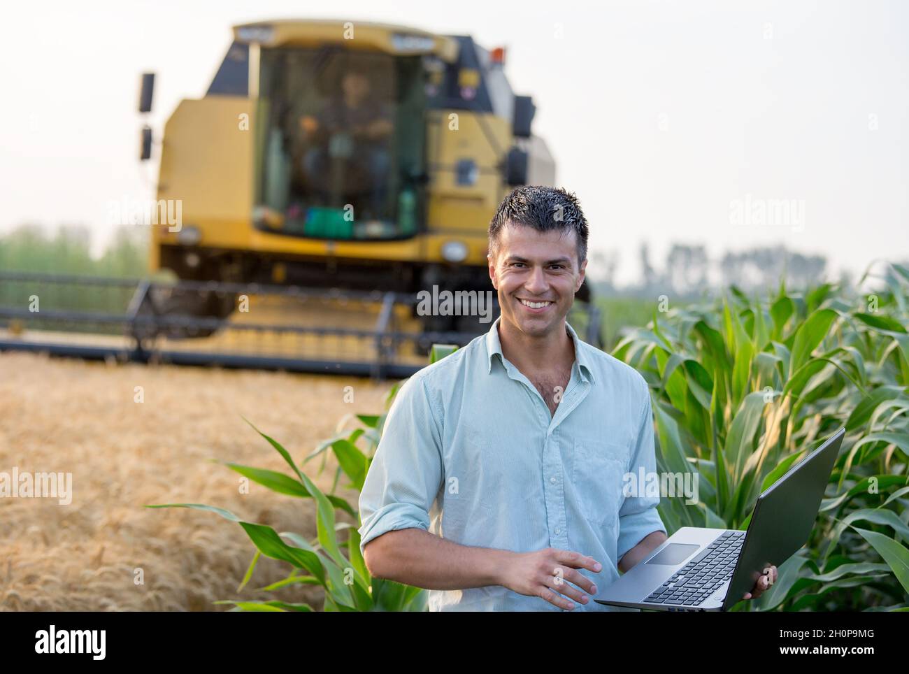 Happy young farmer engineer with laptop standing on wheat and corn ...