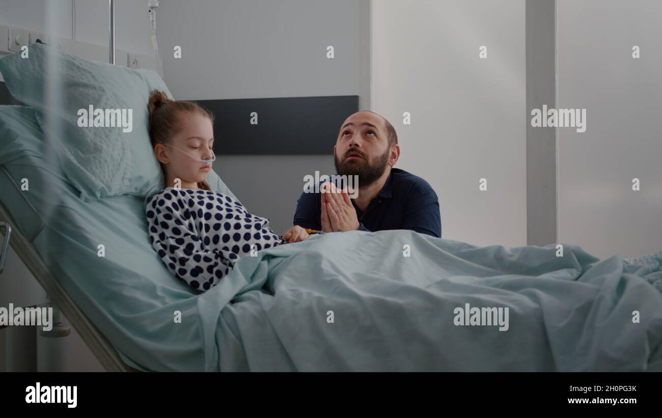 Sick girl daughter sleeping after surgery recovery while worried father praying for kid ...
