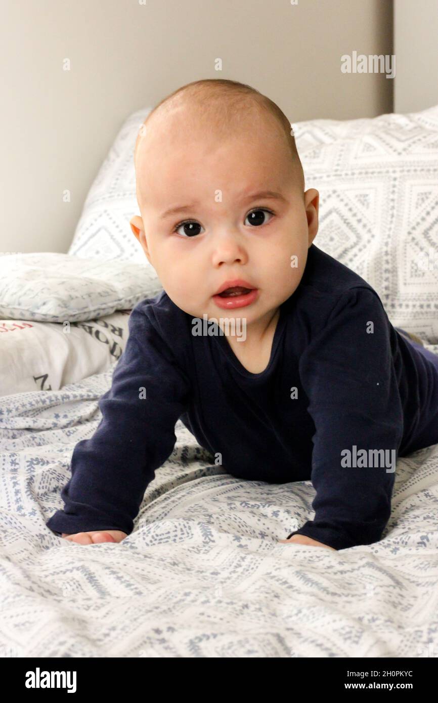 Sweet chubby cheeky baby lying on his tummy on the bed. Funny face ...