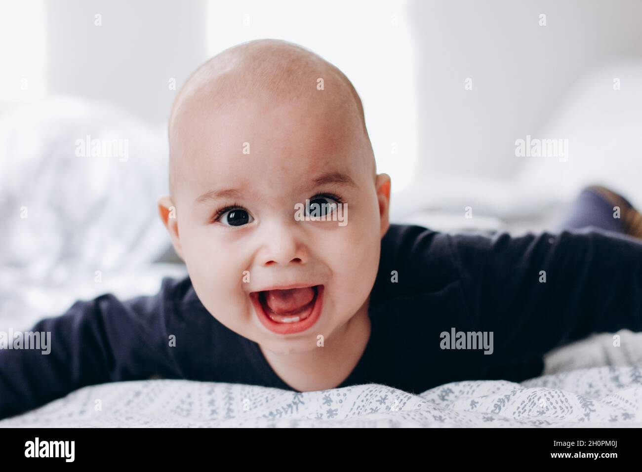 Sweet chubby cheeky baby lying on his tummy on the bed. Funny face ...