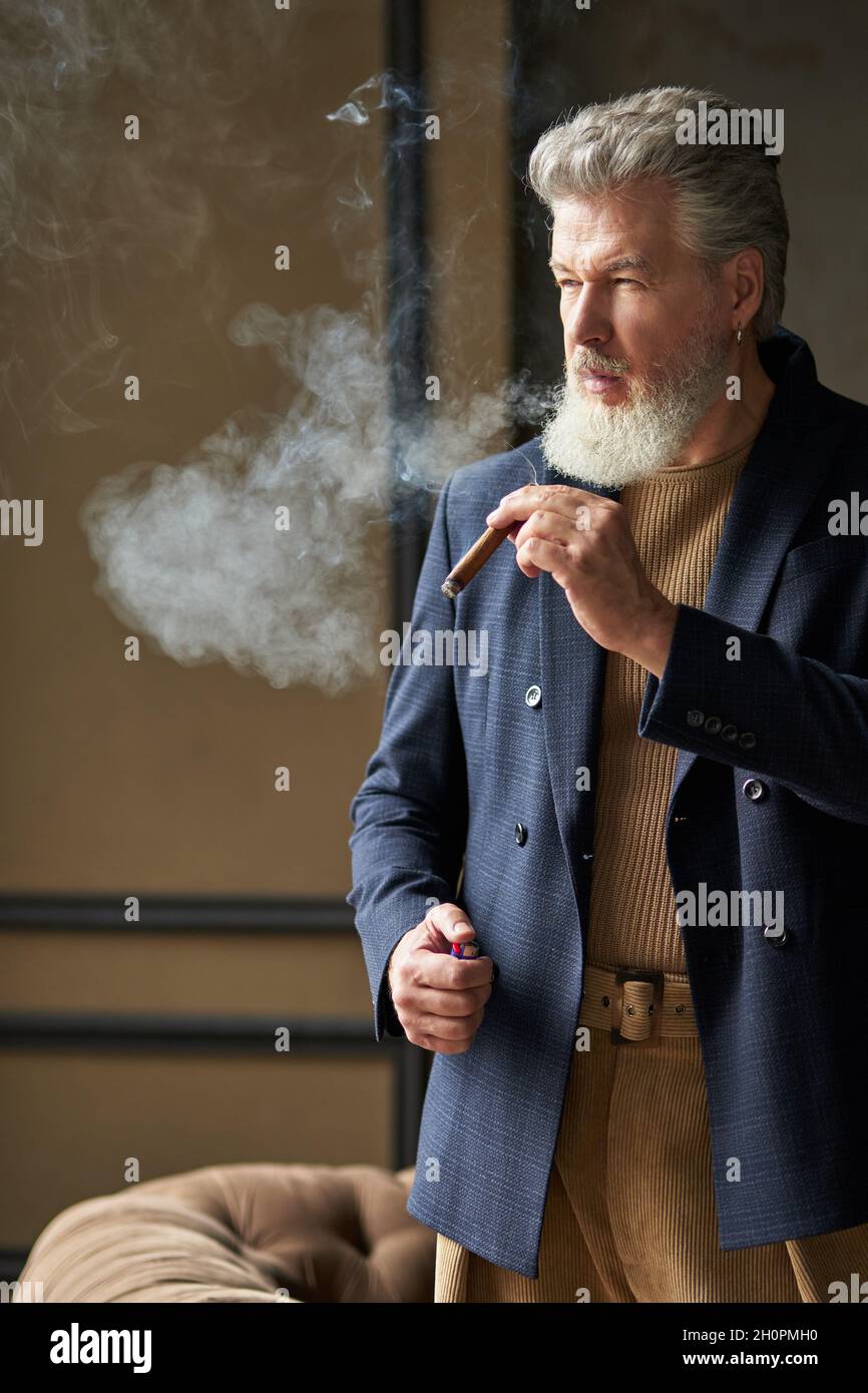 Stylish brutal middle aged man with beard looking away while smoking ...