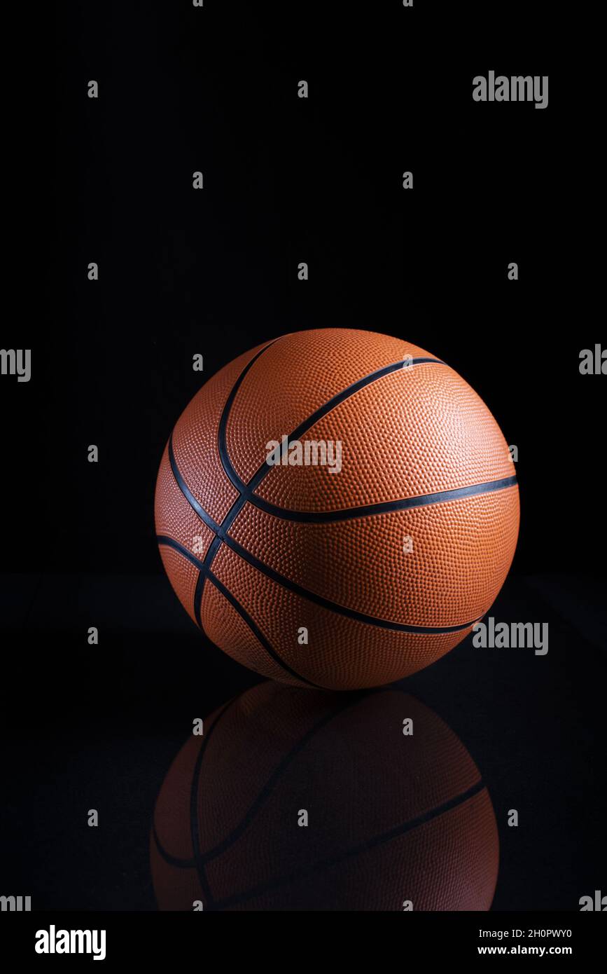 Vertical closeup shot of a brown basketball ball with lines on a black ...
