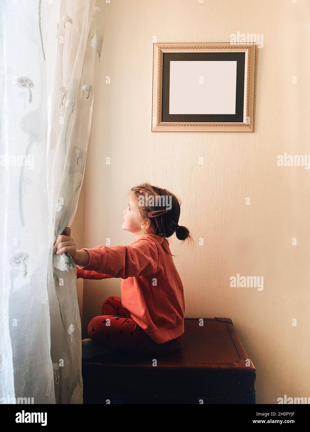 Side view of cute adorable little girl sitting by window and smiling ...
