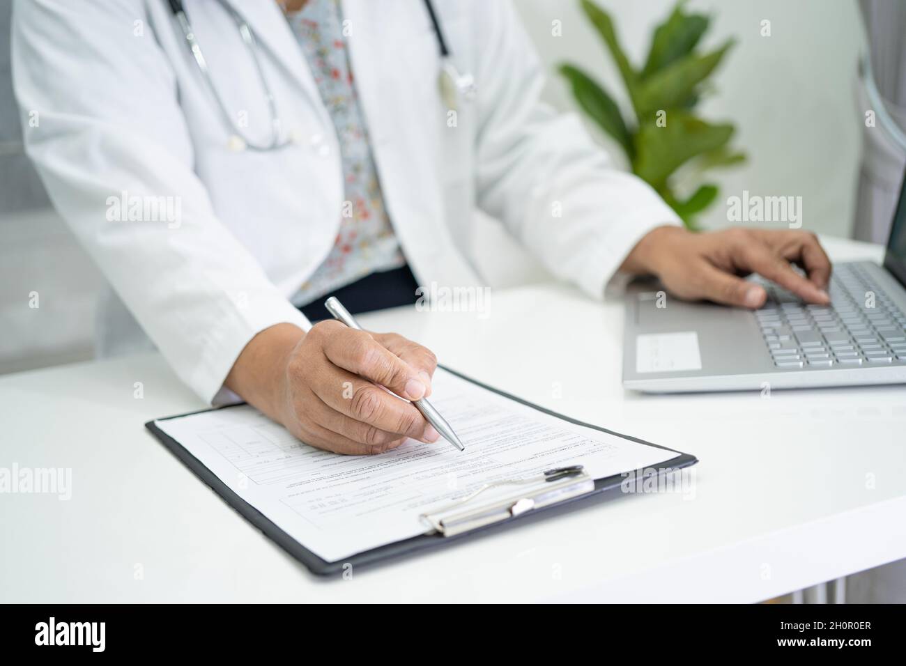 Doctor writing down the diagnosis on clipboard with laptop in nursing ...