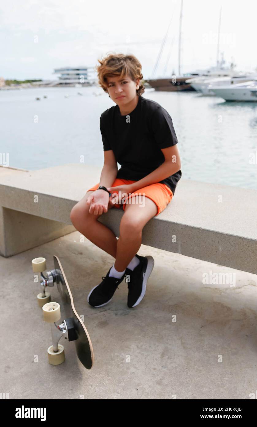 Vertical shot of a young boy model skater sitting on a bench at the ...