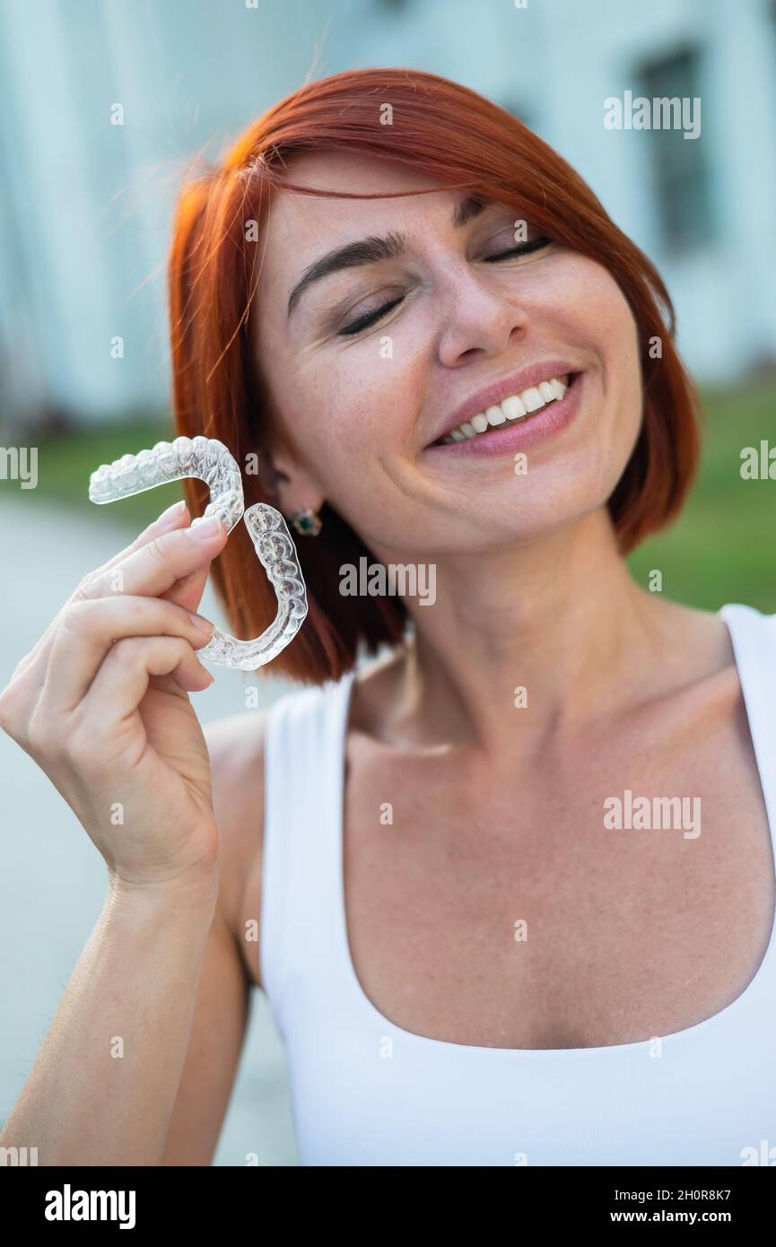 Red-haired Caucasian woman holding transparent mouthguards for bite ...