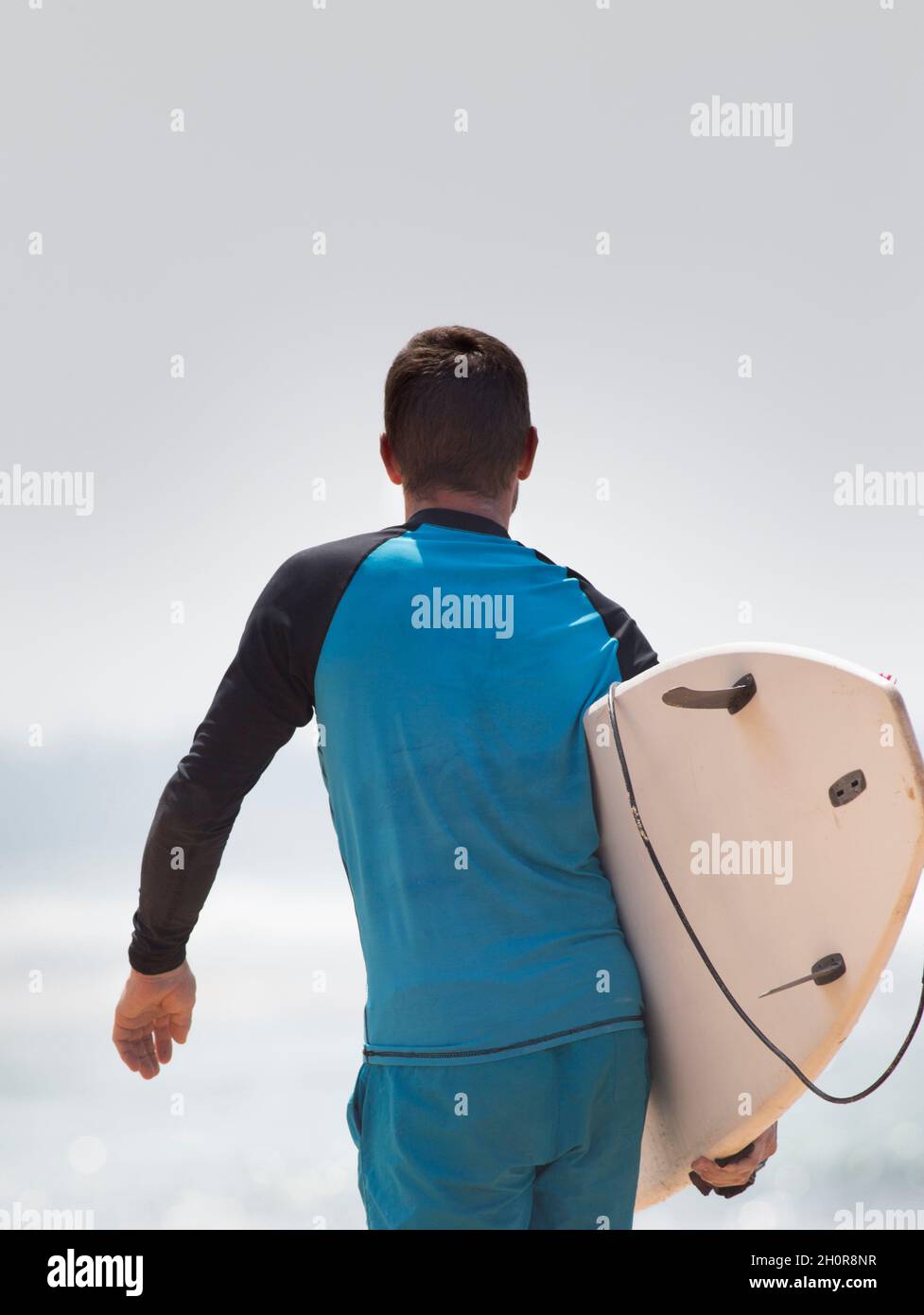Rear view of handsome man carrying surfboard on beach to water Stock ...