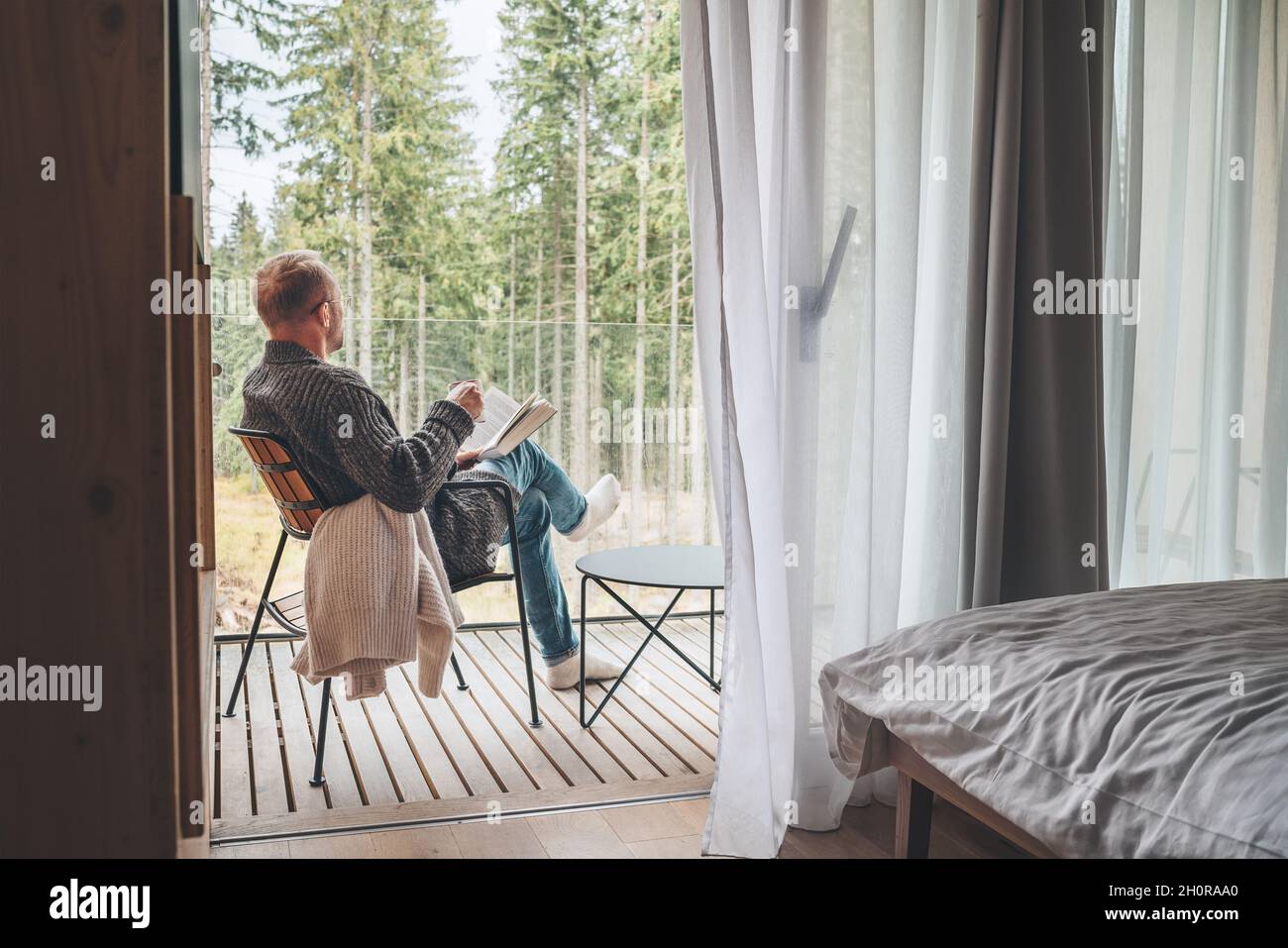 Alone man sitting in chair on country house balcony and enjoying forest ...