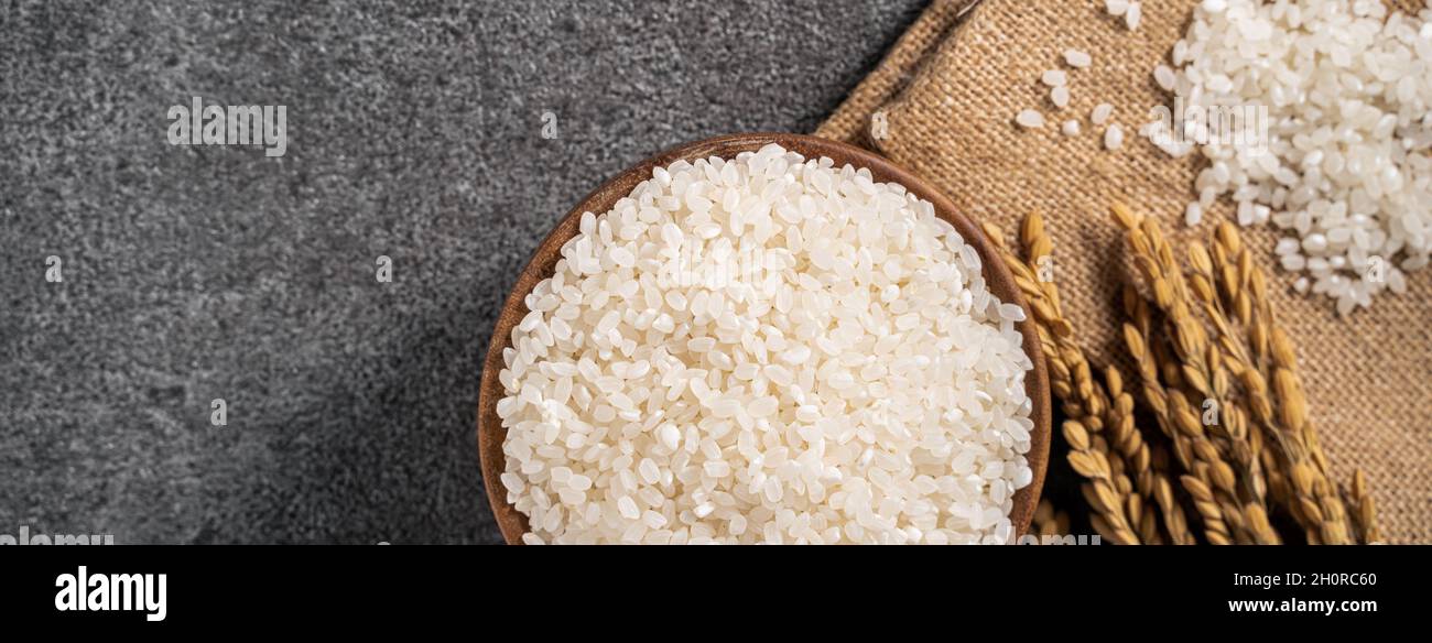 White raw rice in a bowl with the ear on the dark black table ...