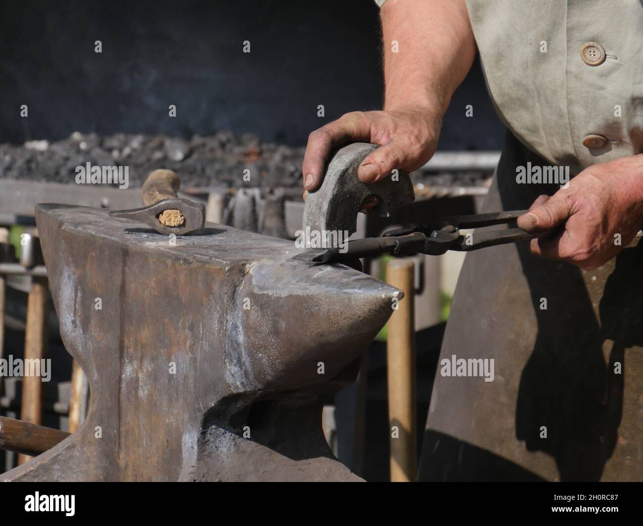 steel anvil, on top of which lies a hot workpiece which is held by a ...