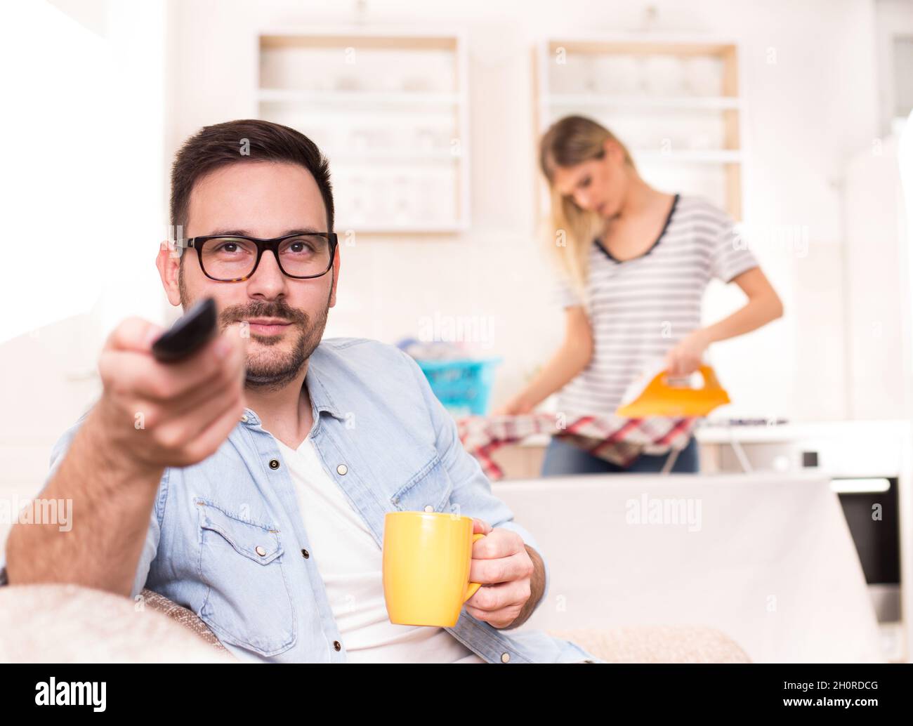 Young handsome man sitting on sofa and holding tv remote control while ...