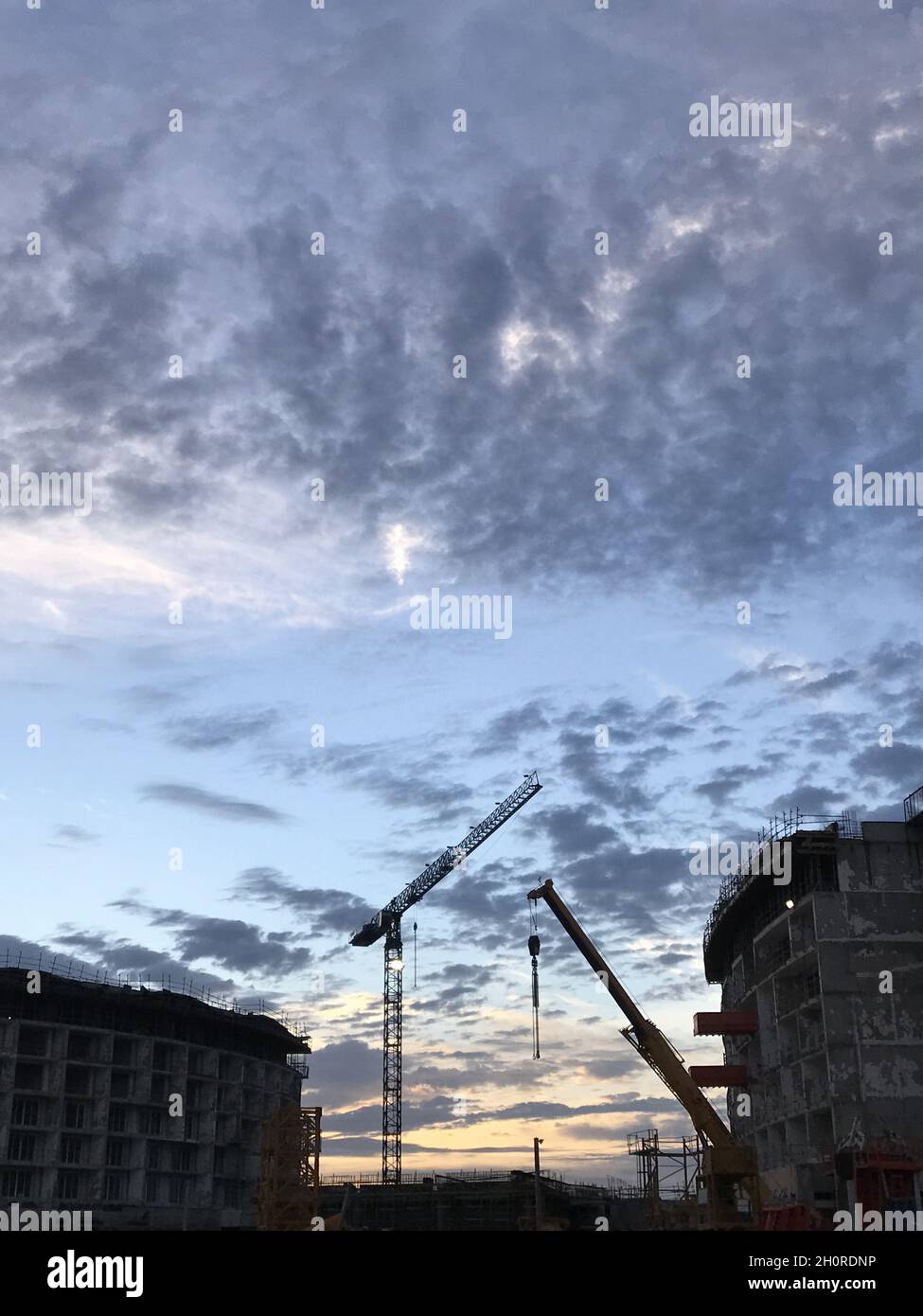 Vertical shot of highrise buildings and tower cranes under a cloudy sky ...