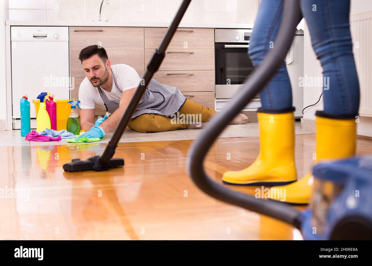 Young couple doing chores together. Man wiping floor on knees and girl ...