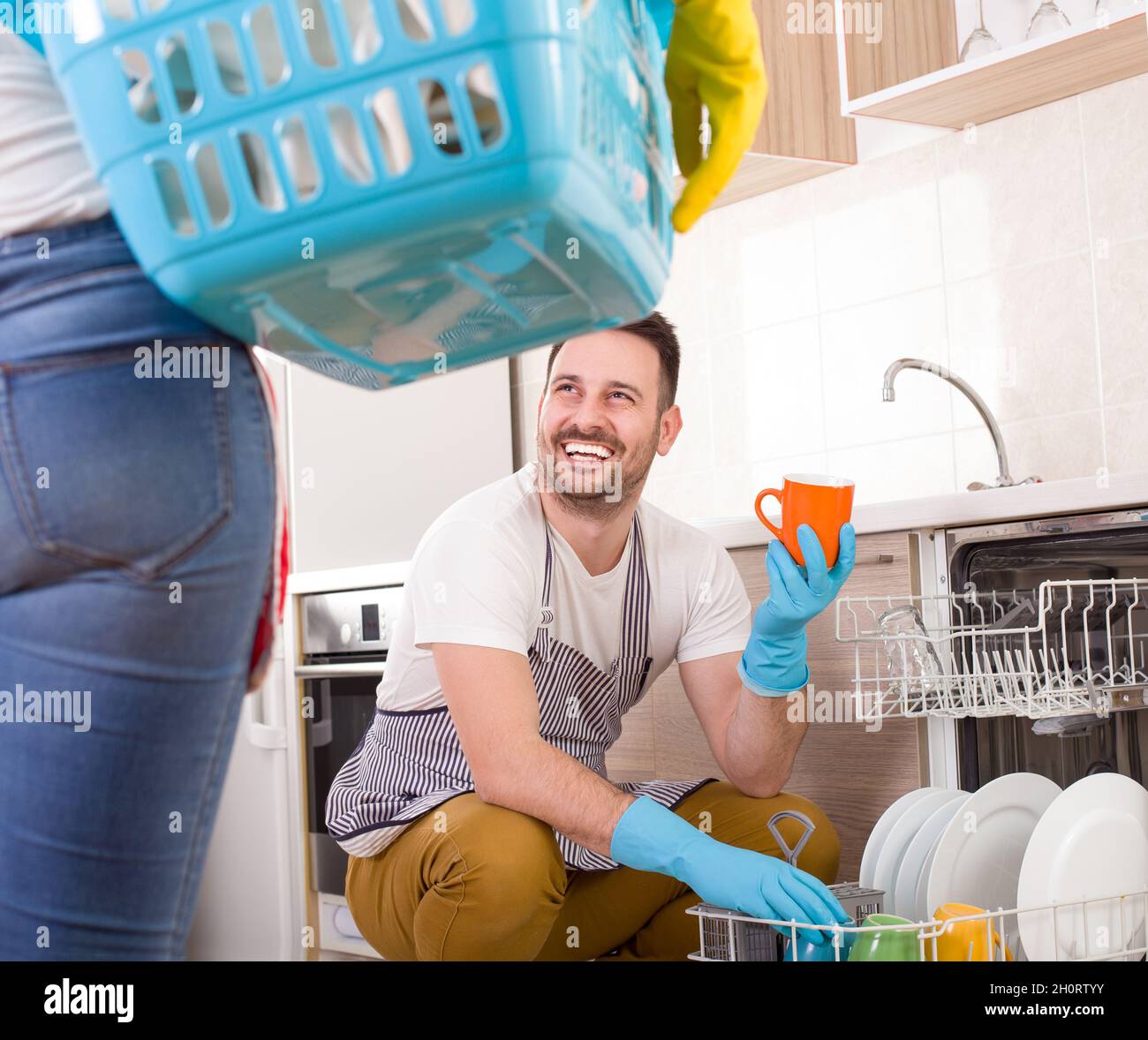Young couple doing chores together. Man loading dishwasher and wife ...