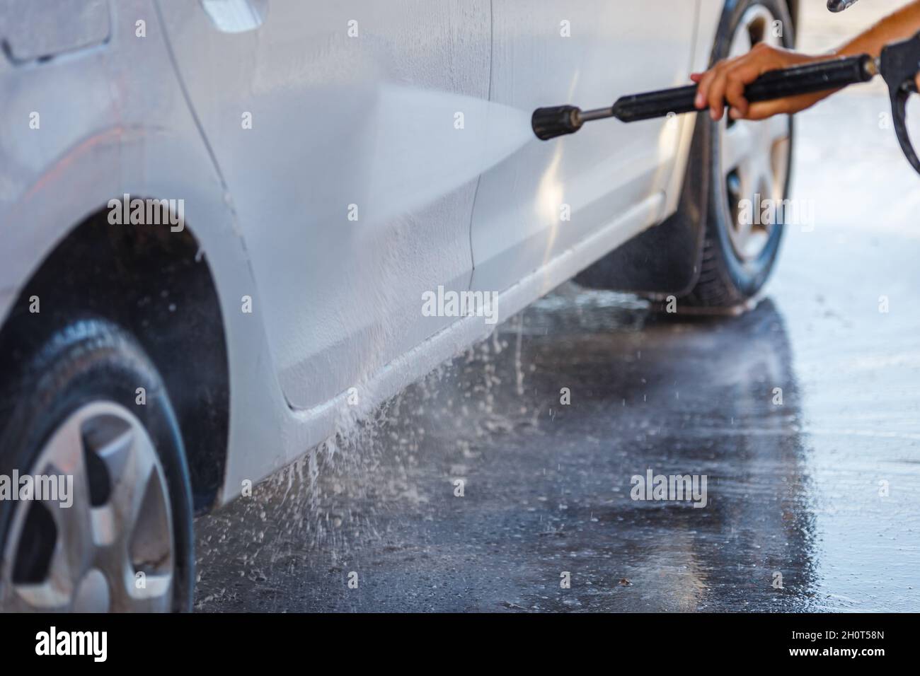 hand with high pressure washer washing white car at public self service ...