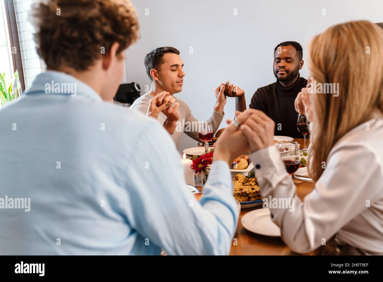 Multiracial friends holding hands and praying during thanksgiving ...