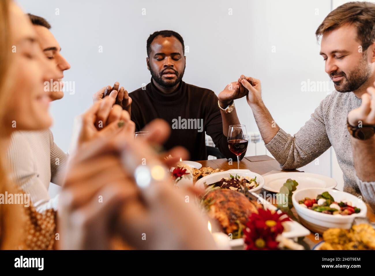 Multiracial friends holding hands and praying during thanksgiving ...