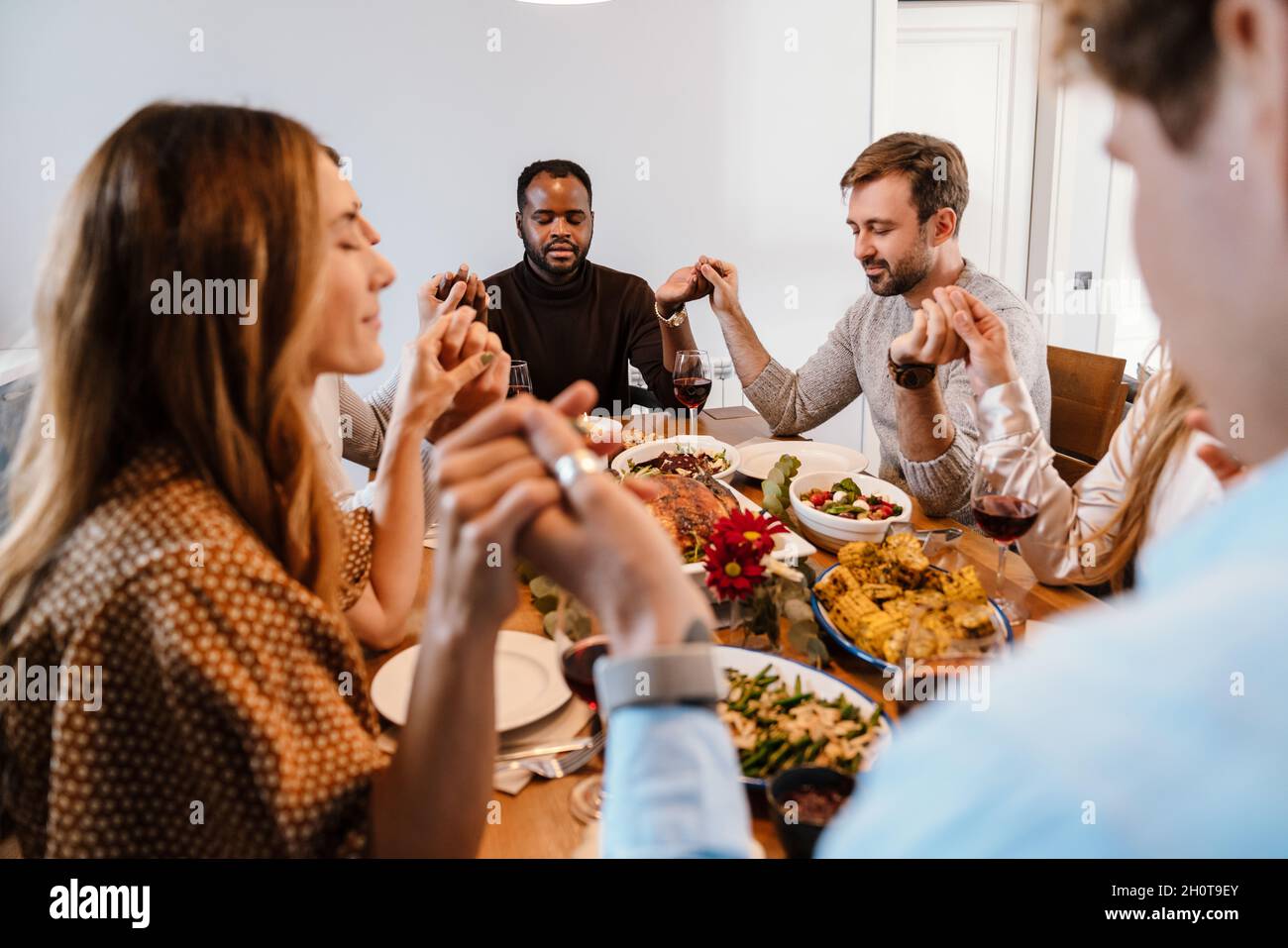 Multiracial friends holding hands and praying during thanksgiving ...