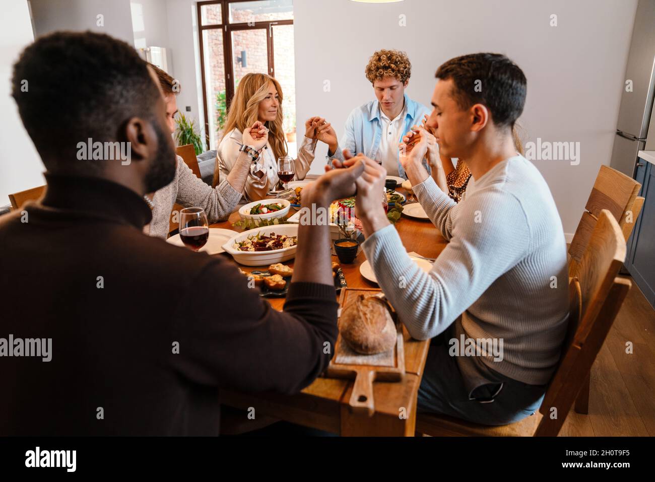 Multiracial friends holding hands and praying during thanksgiving ...