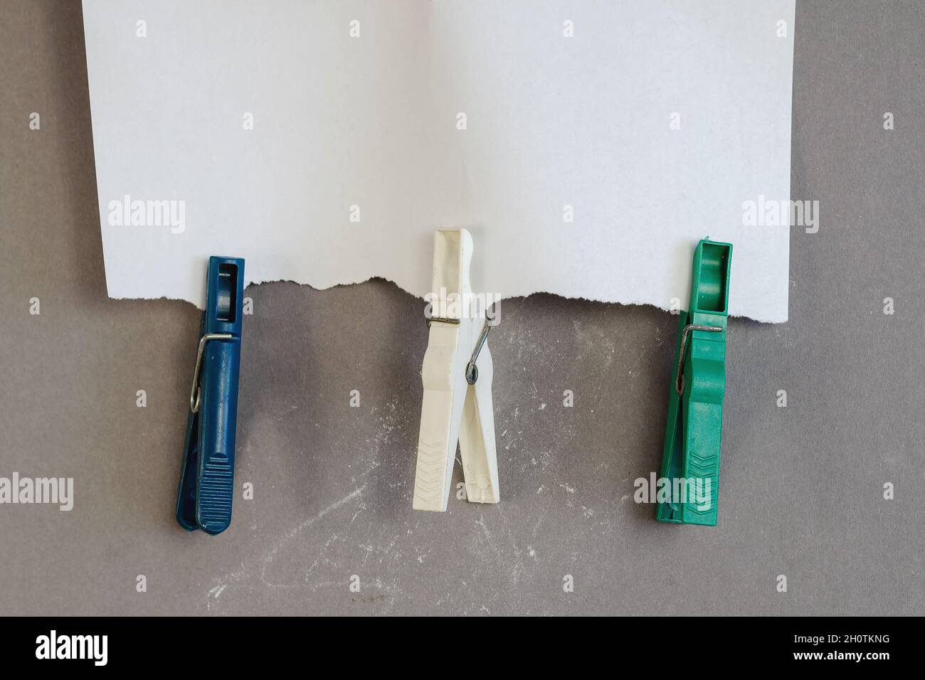 Three plastic clothespins and a white sheet of paper against a gray ...
