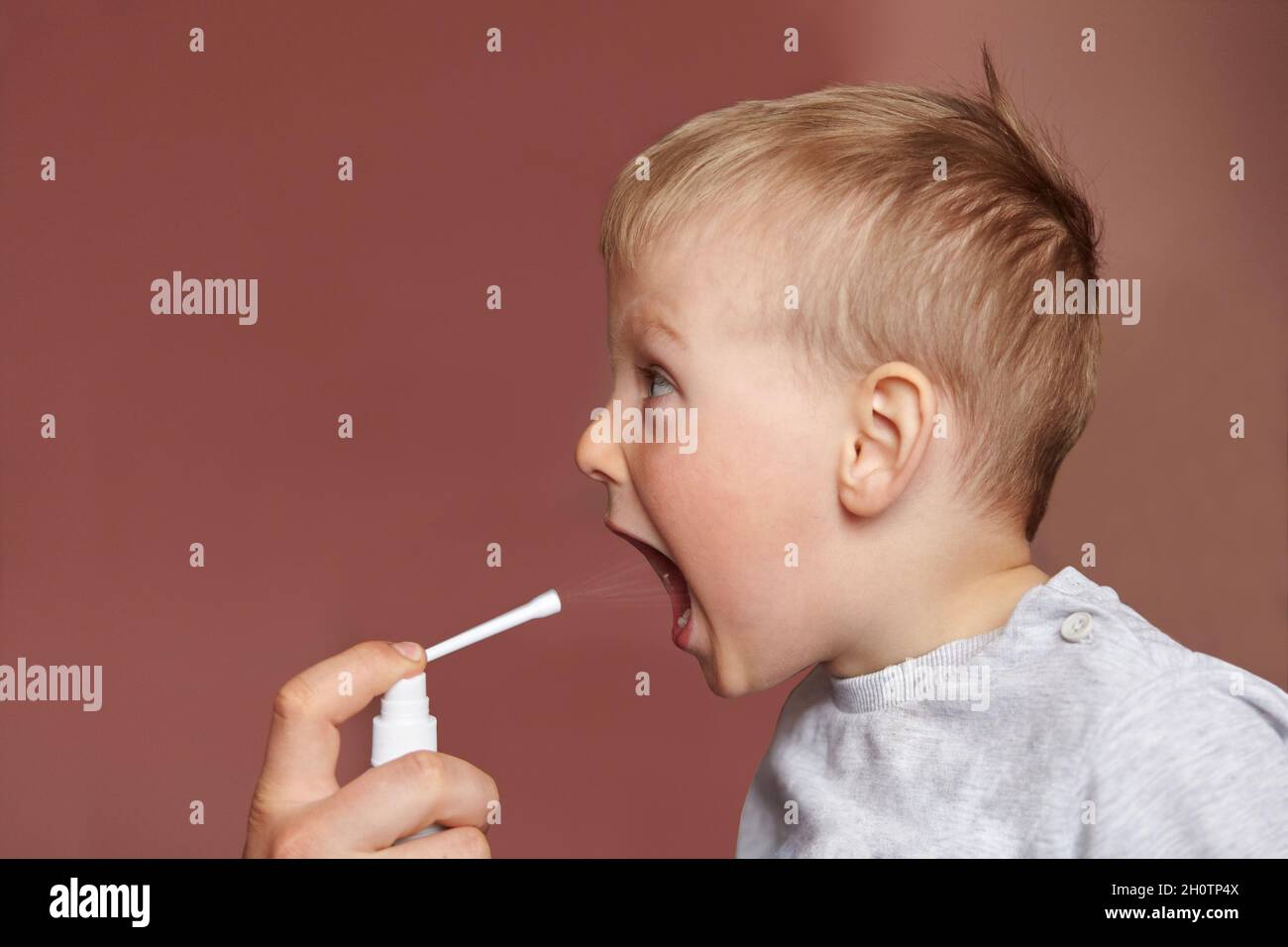 The child receives medication through a mouth spray for a sore throat ...
