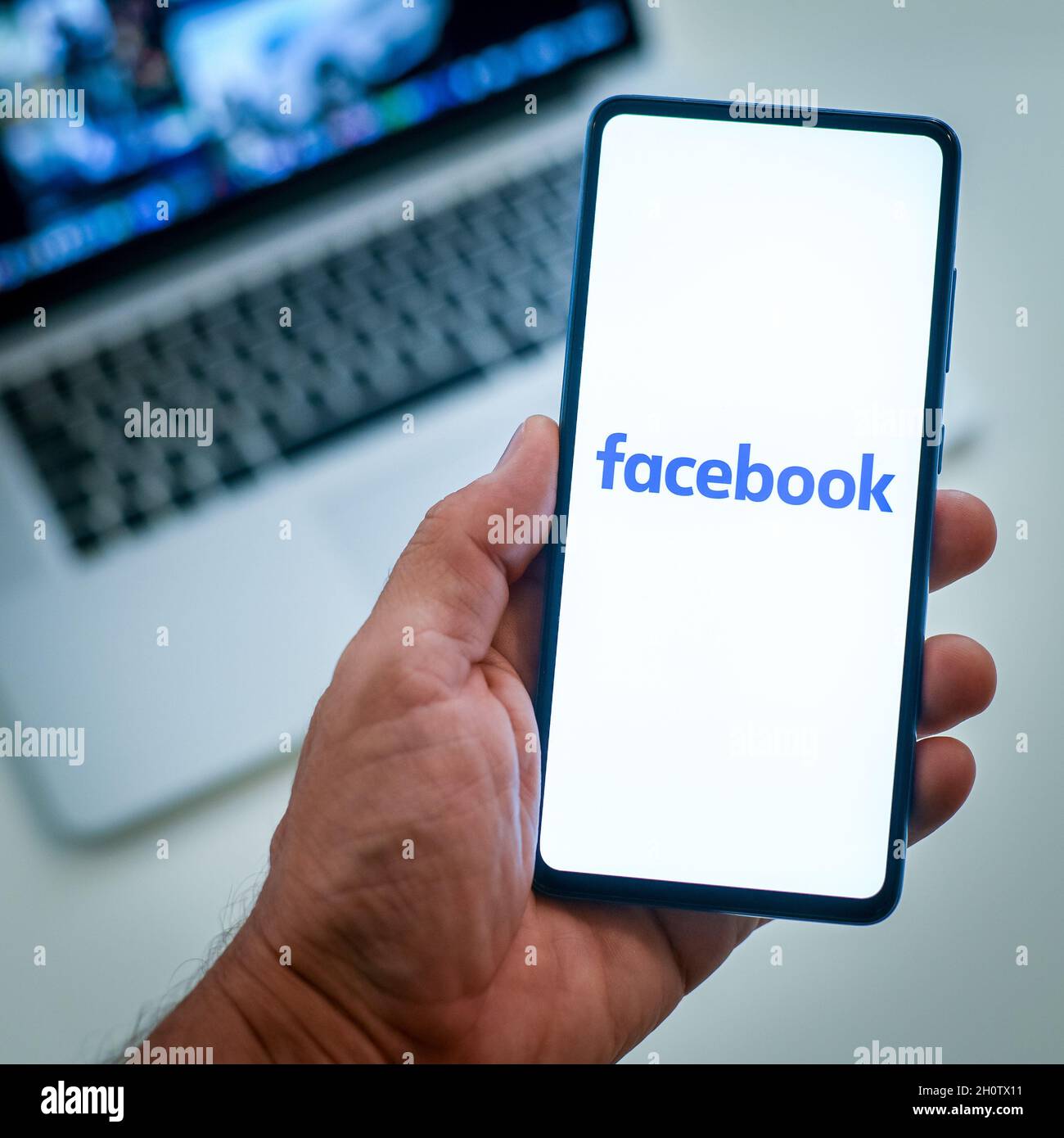 Close up view of hand with smartphone and Facebook logo on display ...