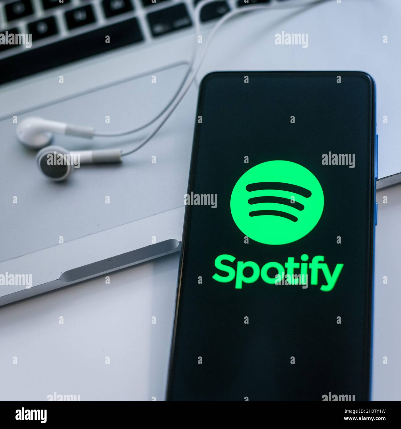 Close up view of a smartphone with Spotify logo on display. Laptop and ...