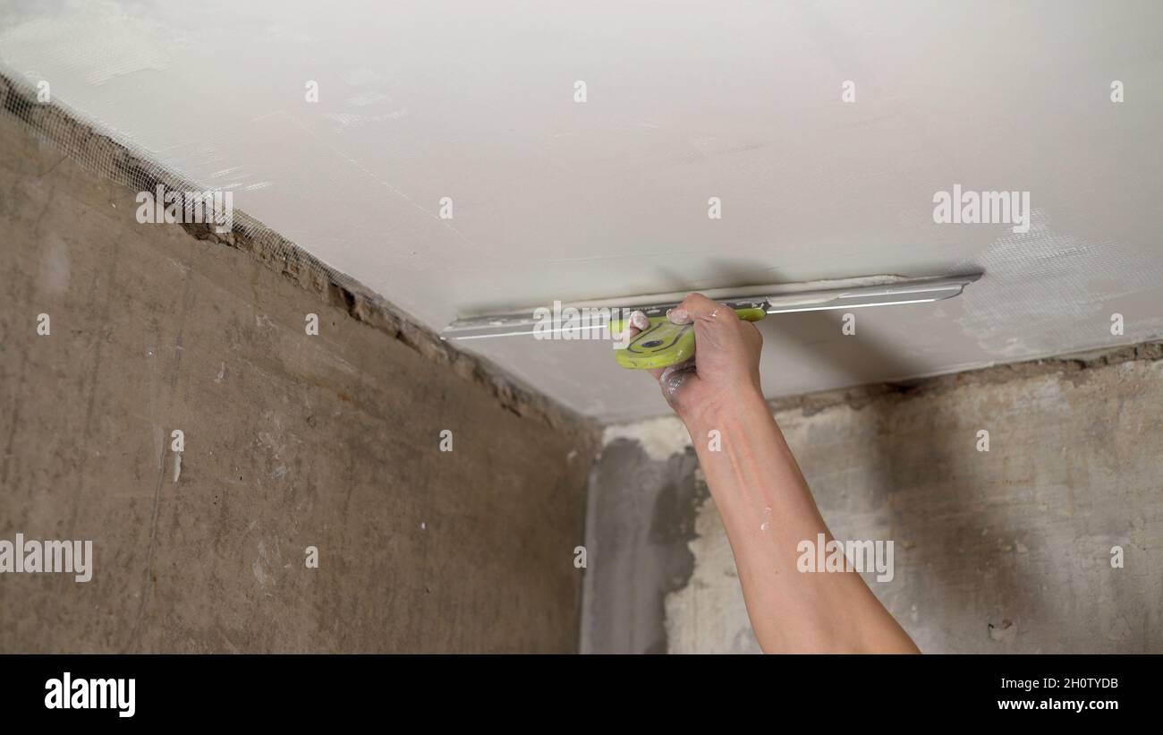 Applying putty to the ceiling with a spatula. A man puts putty on the ...