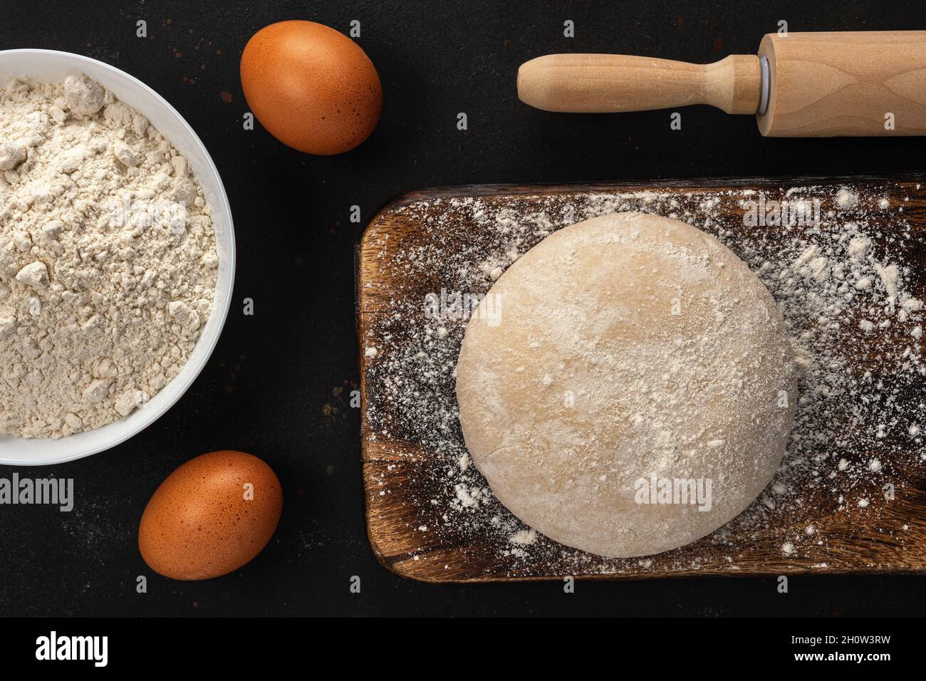 Fresh raw dough for bread or pizza with eggs on a dark background with ...