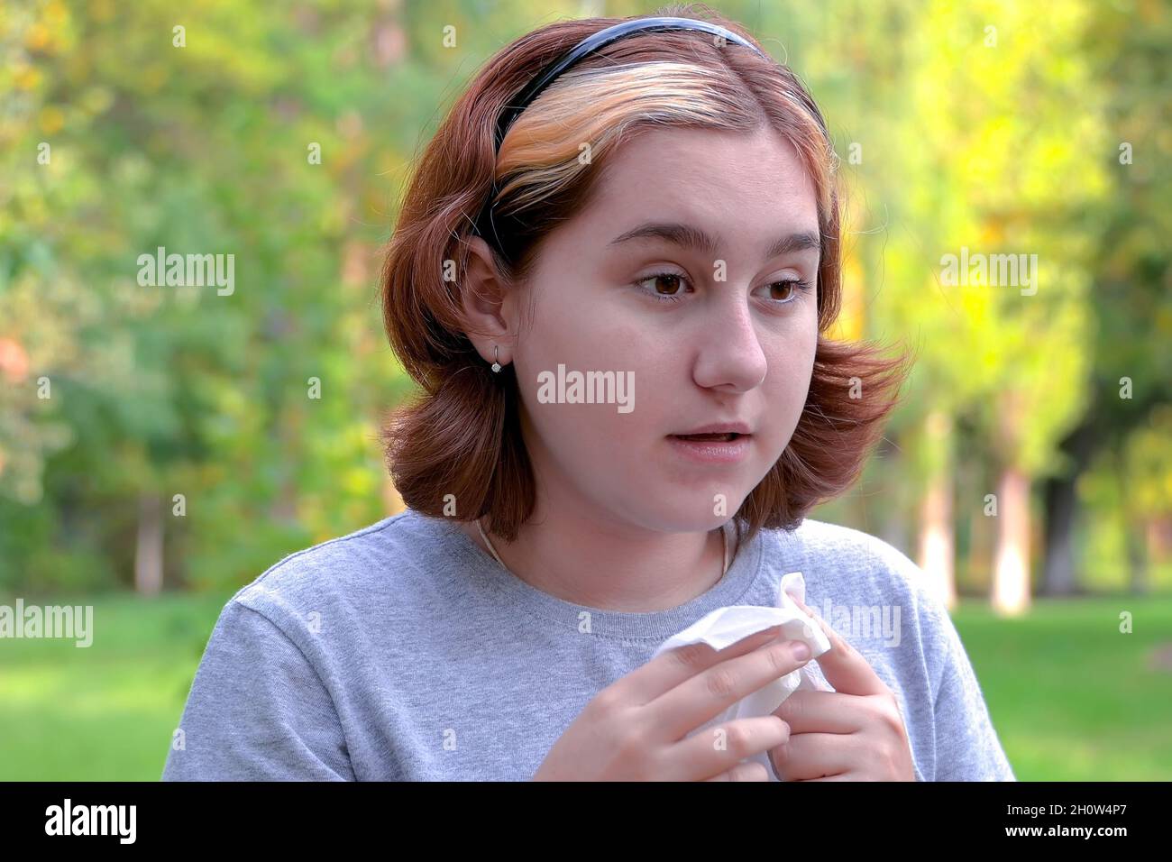 A young girl with allergies in an autumn park. Sneezing girl with a ...