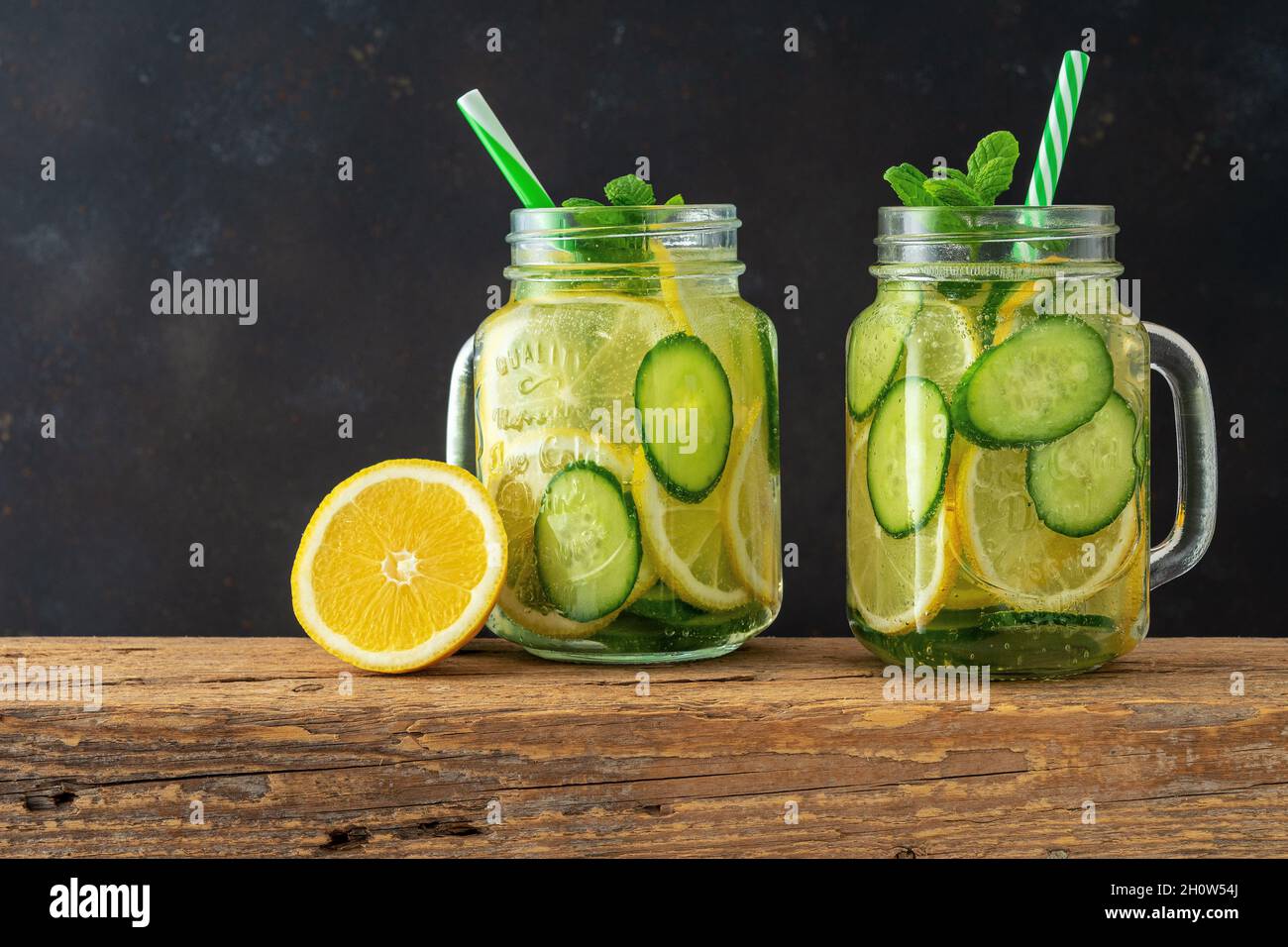 Detox water with sliced lemon and cucumber in a jar on dark background ...