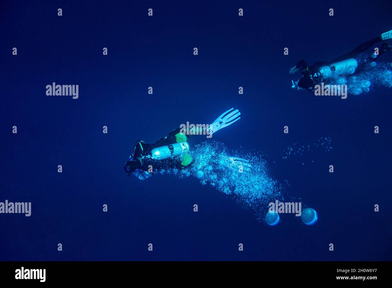 Two scuba divers swimming in deep blue seen from top making bubbles ...