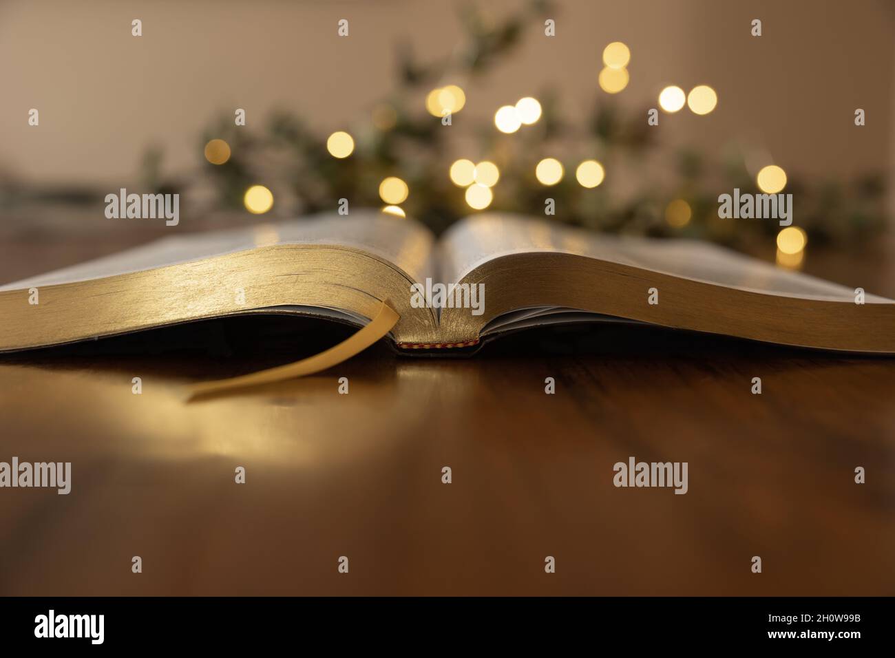 Open bible with gold binding on a dark wood table with garland and ...